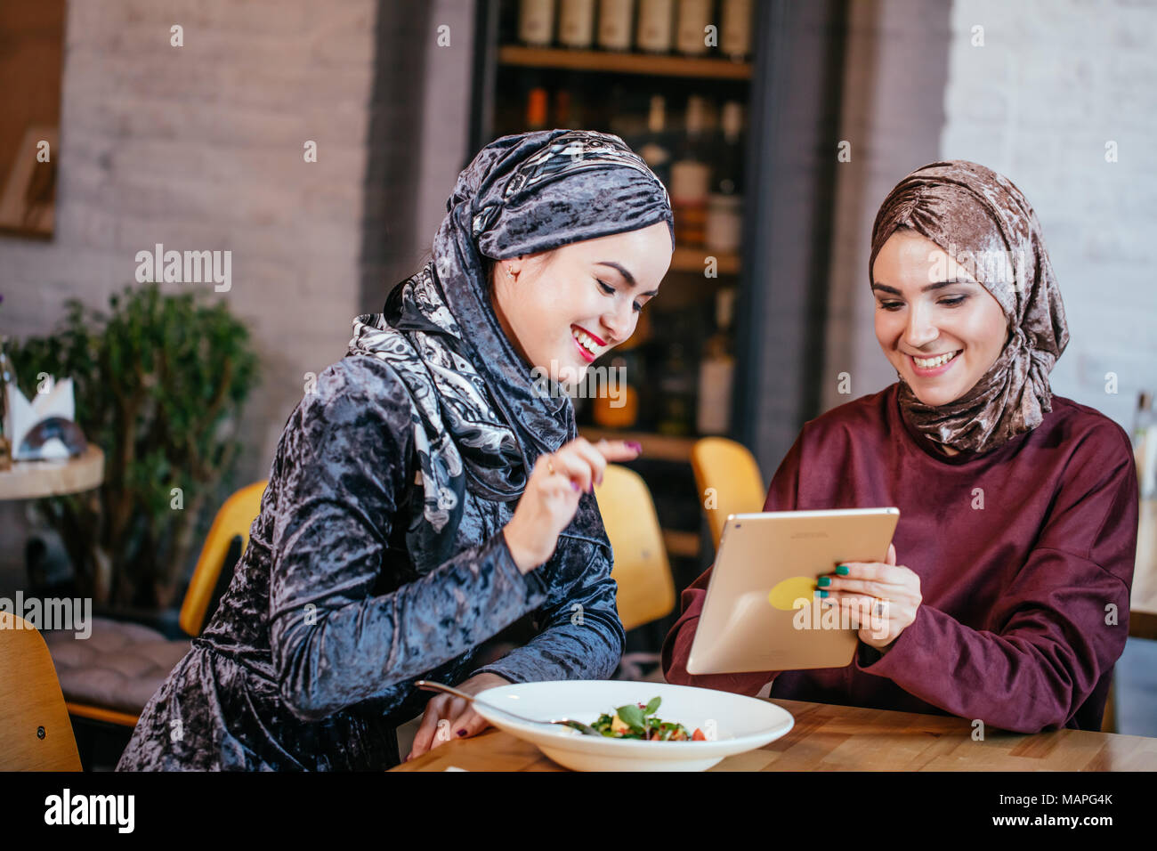 Two Muslim women in cafe, shop online using electronic tablet Stock ...