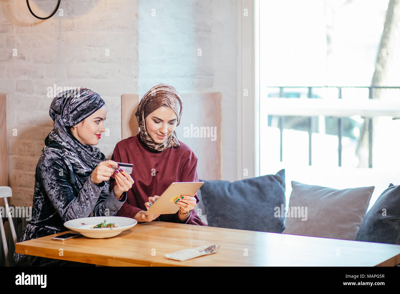 Two Muslim women in cafe, shop online using electronic tablet Stock ...