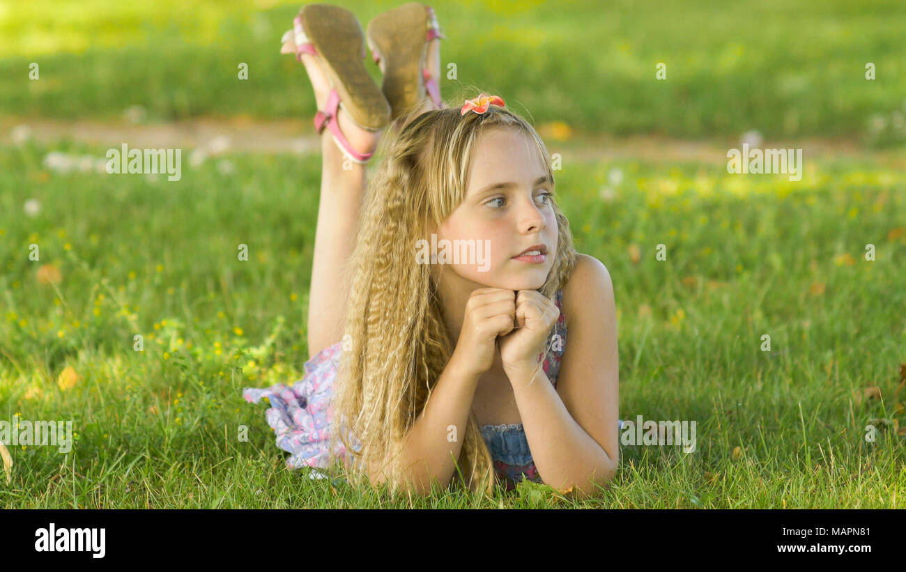 Beautiful young blonde girl lying on a field, green grass. Outdoors ...