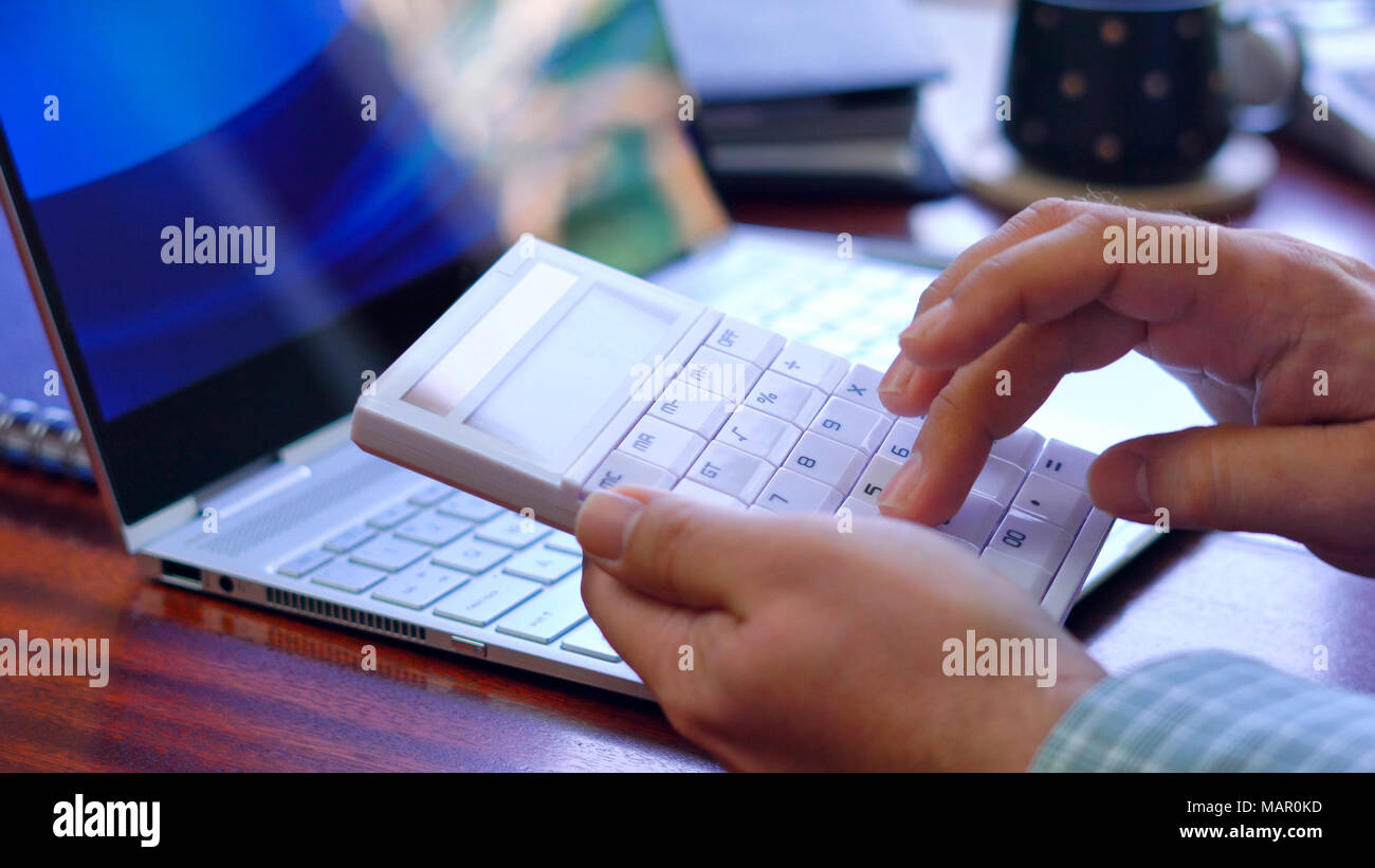 Man using calculator at desk, backlit by sunshine through window, close ...