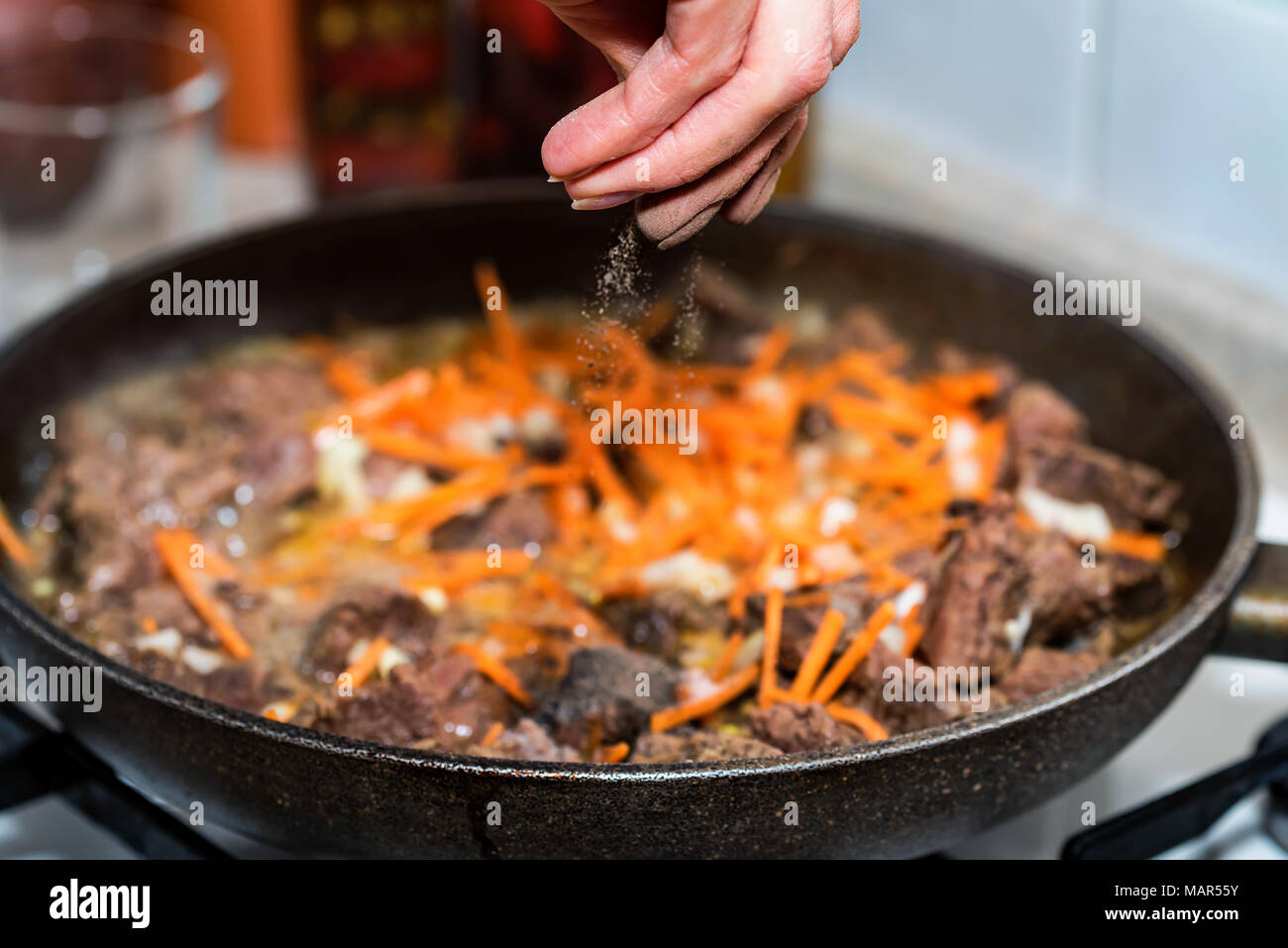 Hand adds salt to beef stew close Stock Photo - Alamy