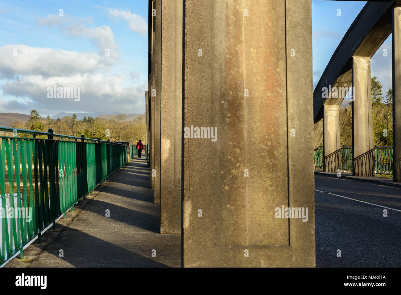Lone person in red jacket walking on bridge along cement columns,The ...