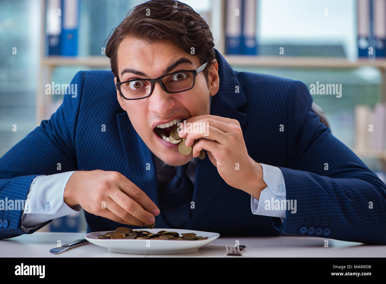 Funny businessman eating gold coins in office Stock Photo - Alamy