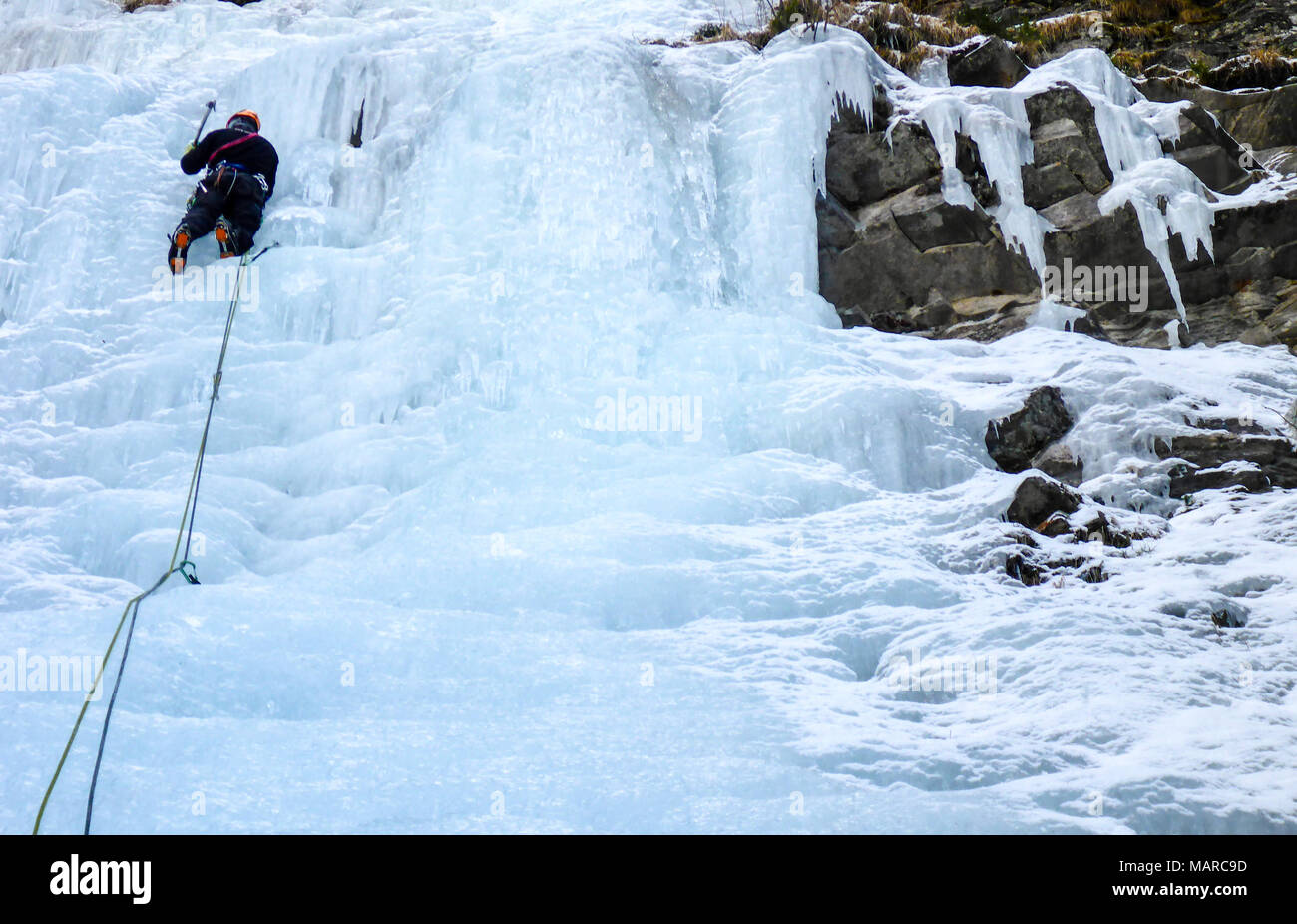 male mountain guide lead ice climbing a frozen waterfall in deep winter ...