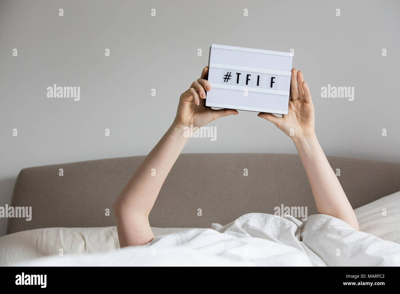 Female in bed under the sheets holding up a TFIF sign Stock Photo - Alamy