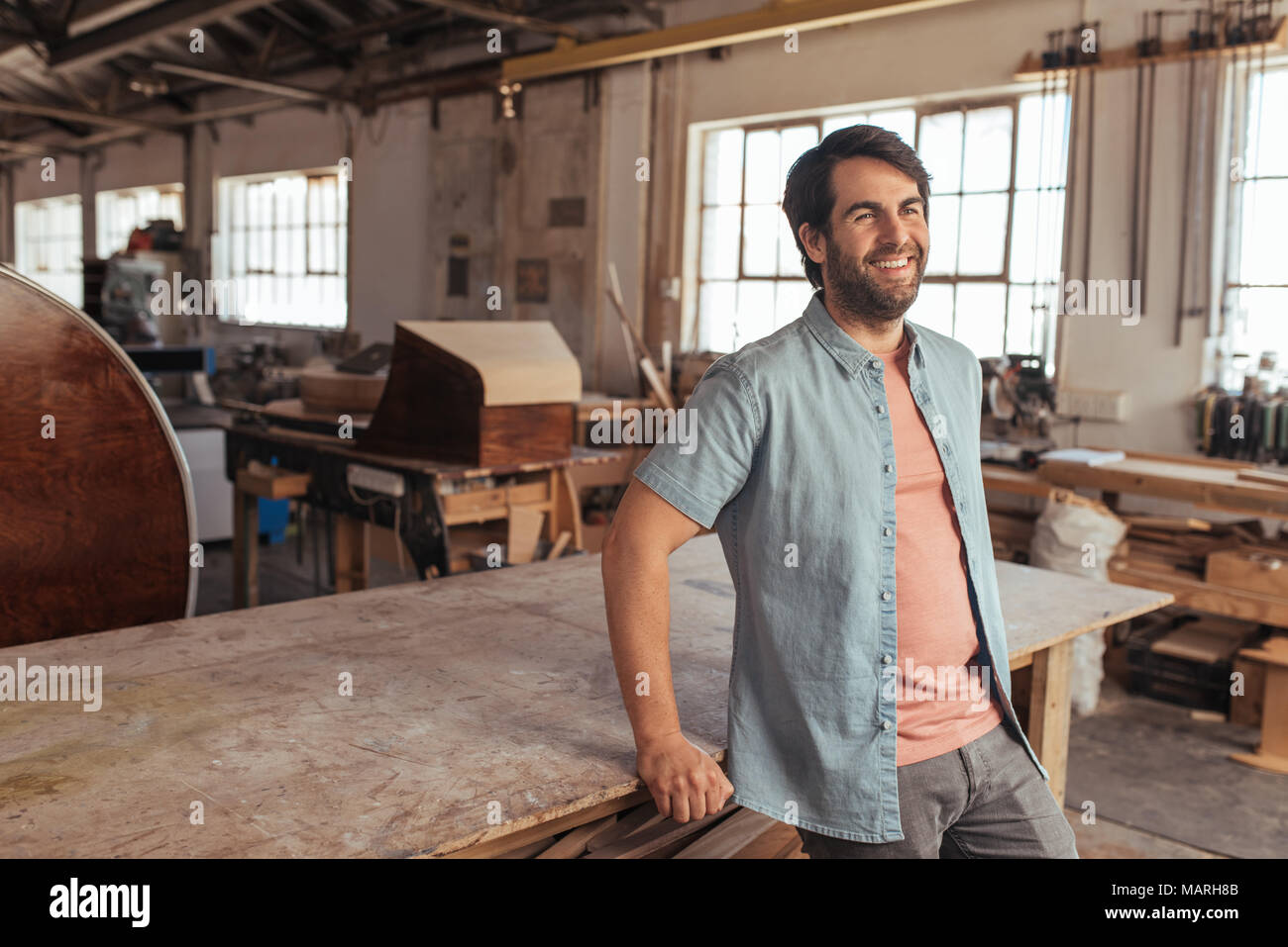Smiling young woodworker leaning on a table in his workshop Stock Photo ...