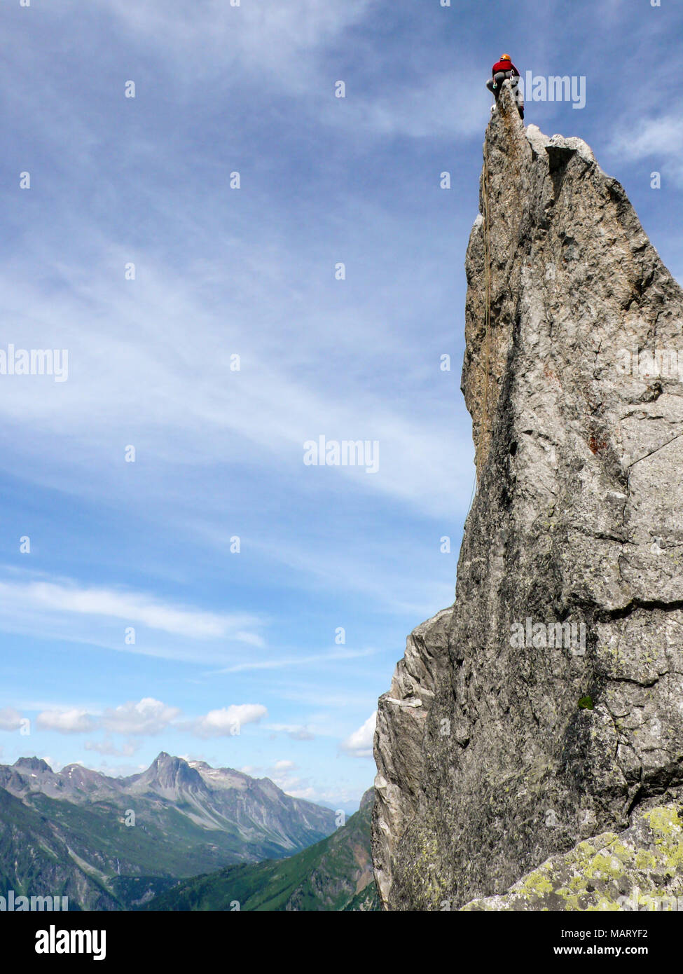rock climber sitting atop a sharp rock needle in the Val Bregaglia ...
