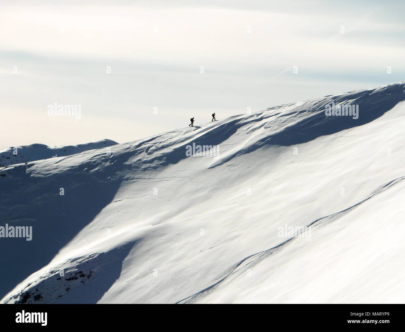 two backcountry skiers hiking up on a long mountain ridge towards the ...