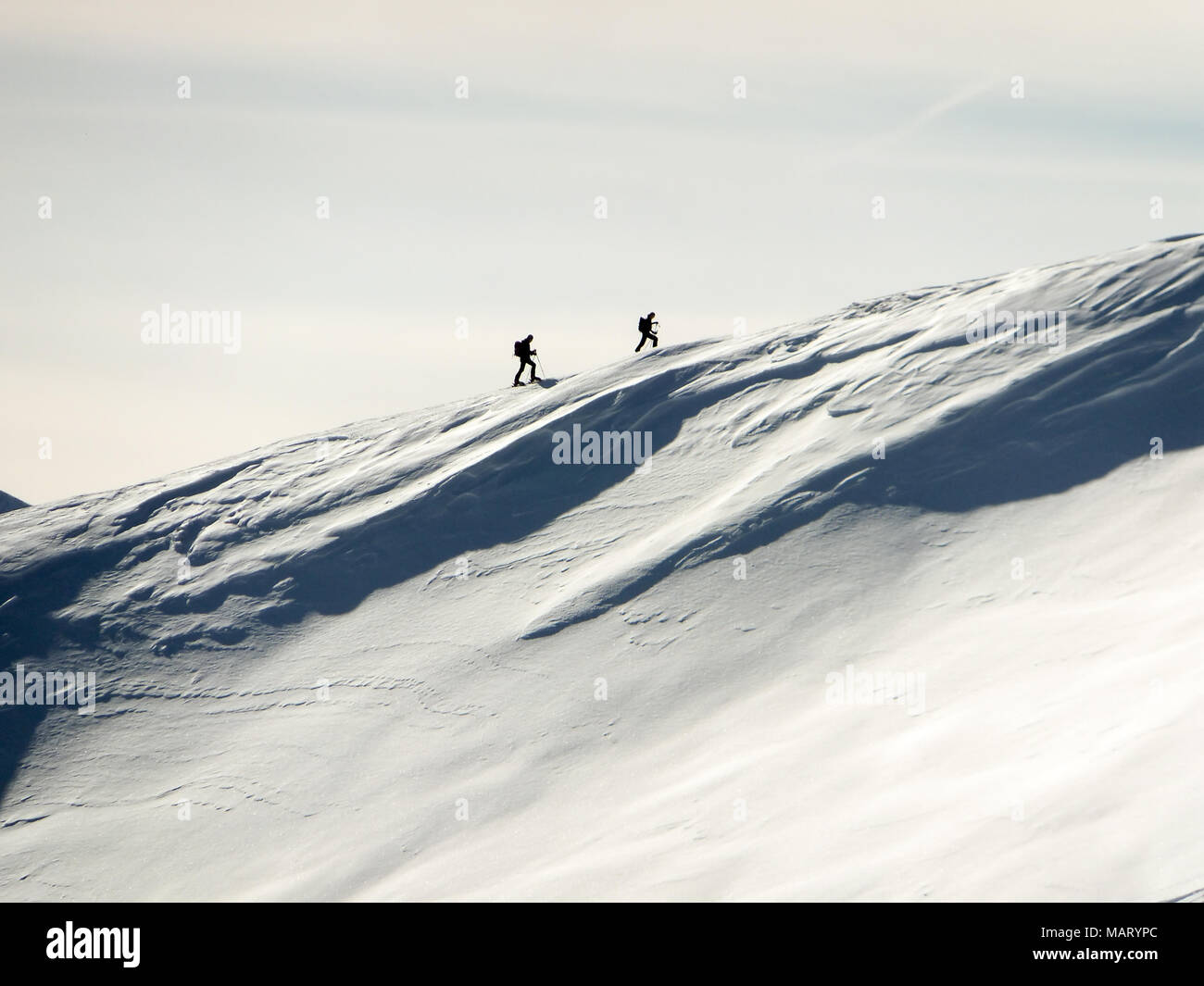 two backcountry skiers hiking up on a long mountain ridge towards the ...