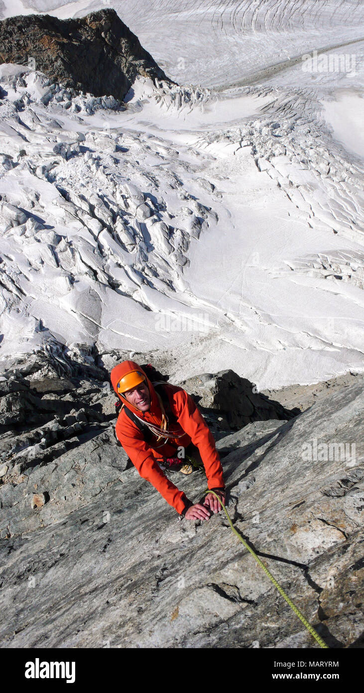 male mountain climber on an exposed climbing route high above a glacier ...