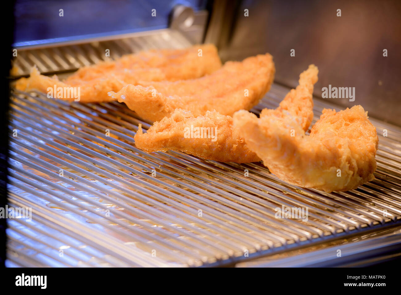 Battered fish keeping warm in a display shelf in a fish and chip shop ...