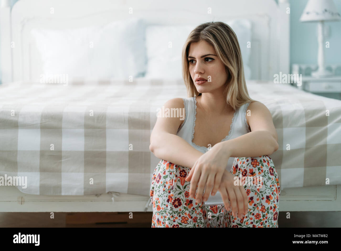 Depressed young woman sitting on bed at home Stock Photo - Alamy