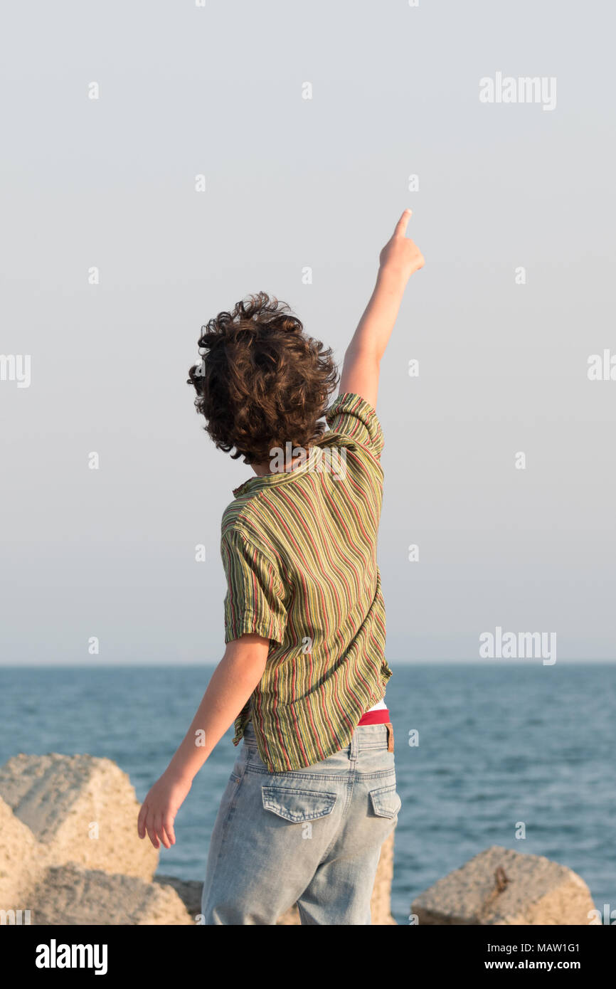 The boy is standing on the pier, facing the sea and pointing his hand ...