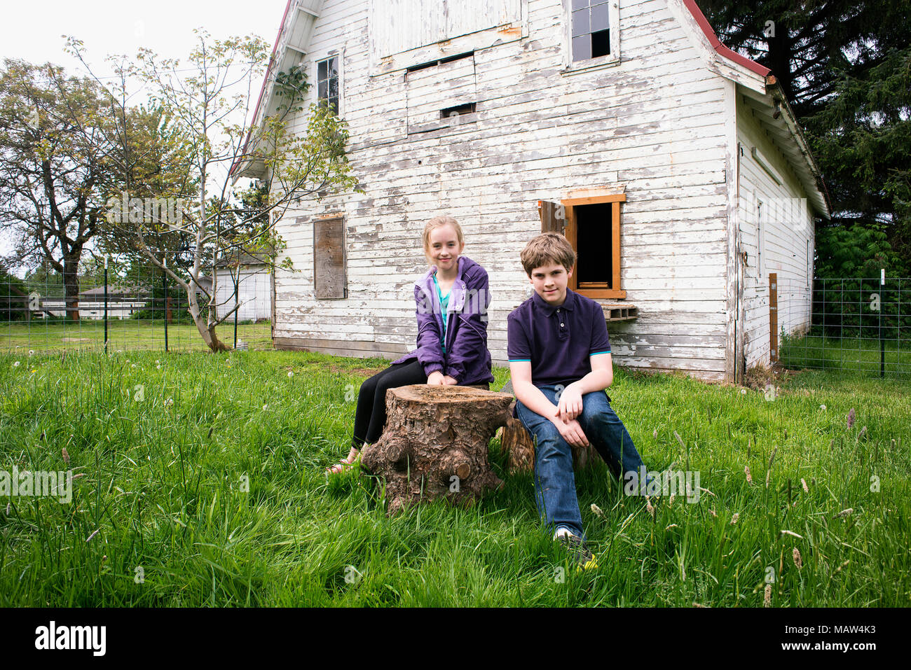 Two children sitting in front of a barn Stock Photo - Alamy