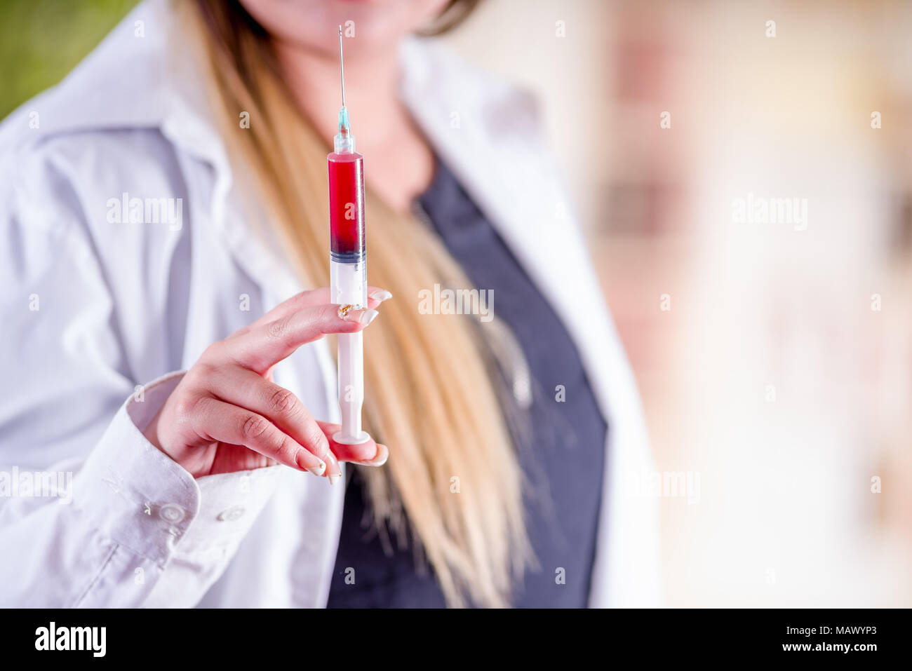 Close up of woman wearing a lab coat and holding a syringe with blood ...