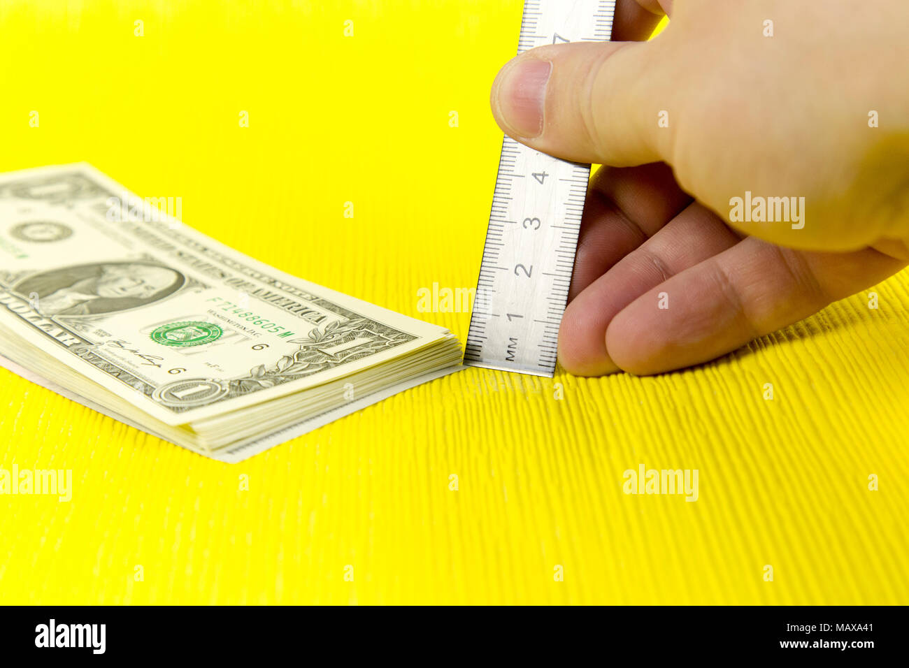 A hand with a ruler measures the thickness of a stack of paper bills ...
