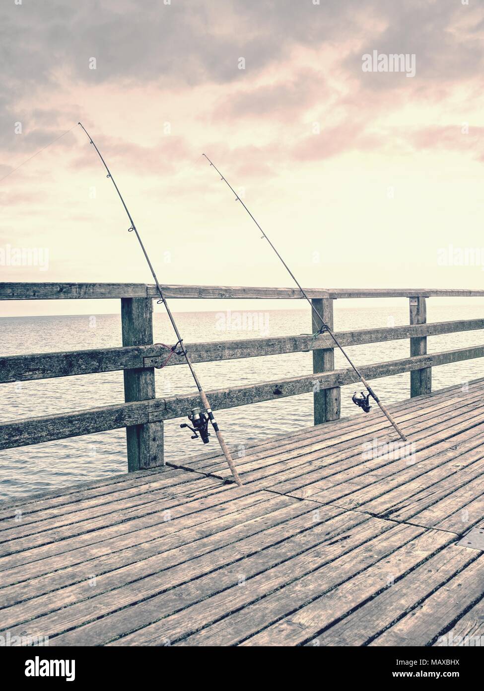 Several fishing rods against the wooden railing of the beach pier ...