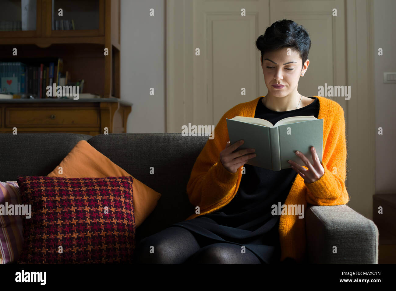 Woman with Short Hair Reading a Book on a Sofa Stock Photo - Alamy