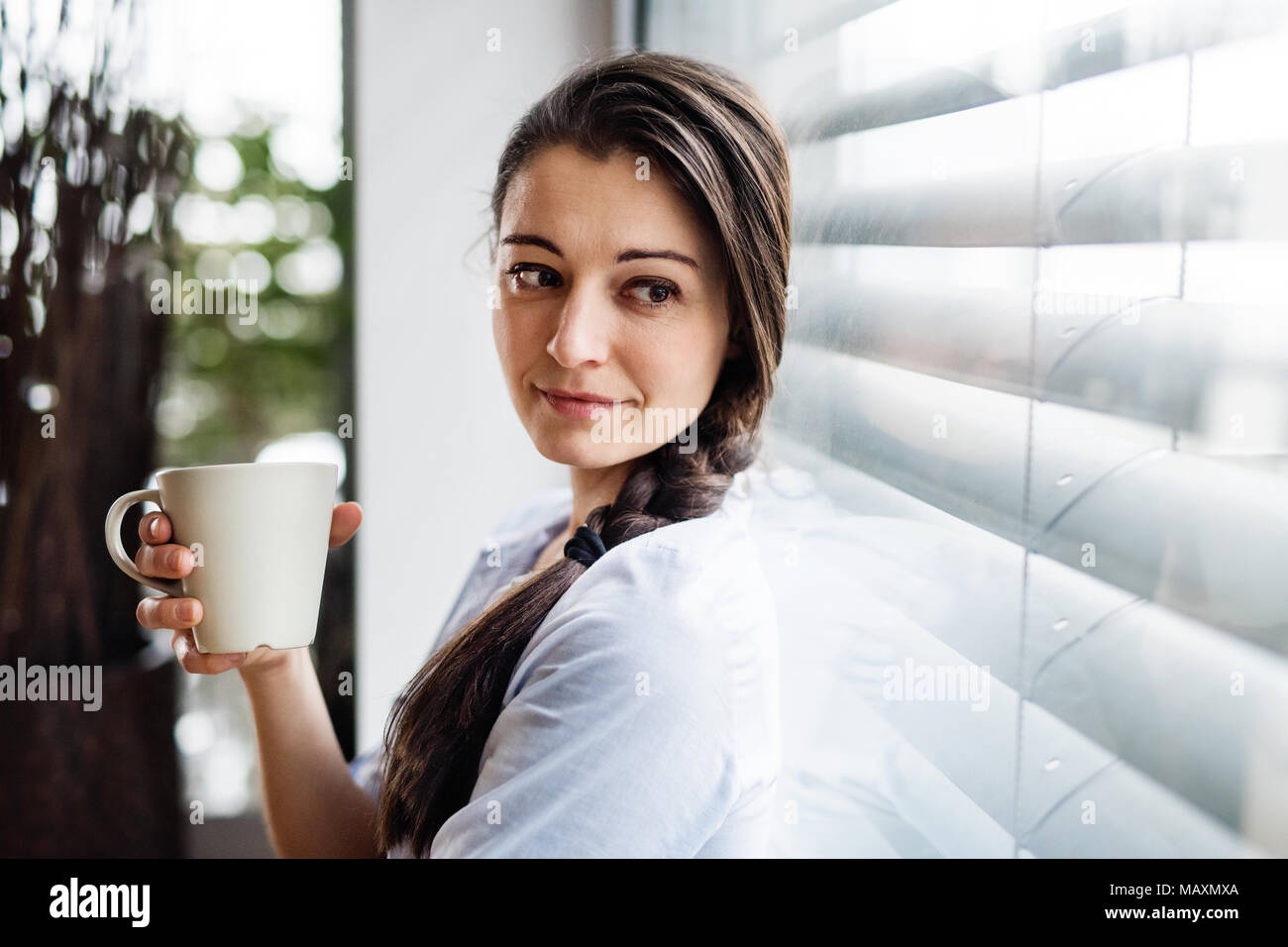 Woman by the window holding cup of coffee Stock Photo - Alamy