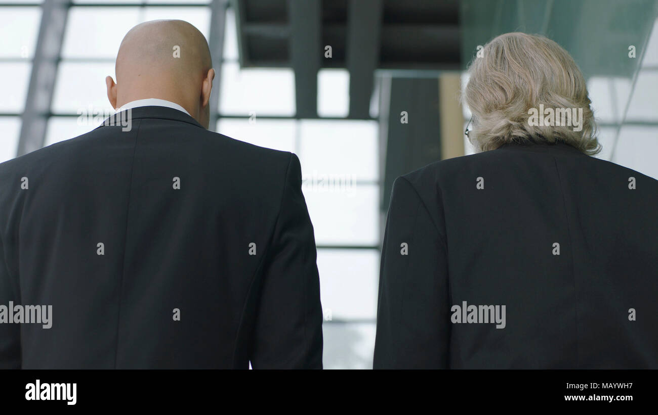 rear view of corporate executives talking while ascending stairs in ...
