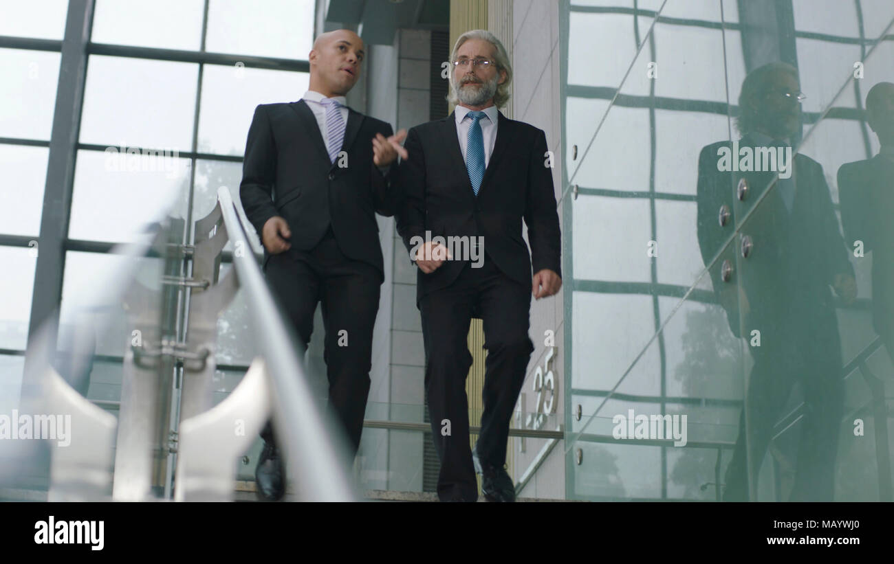 two corporate executives talking while descending stairs in modern ...