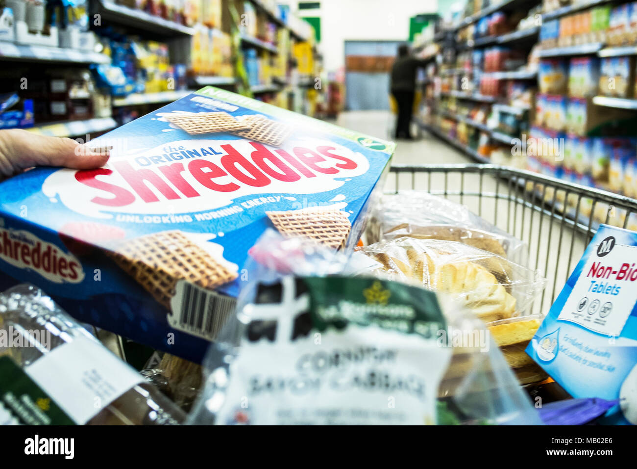 A customer putting a box of cereal into a shopping trolley in a ...
