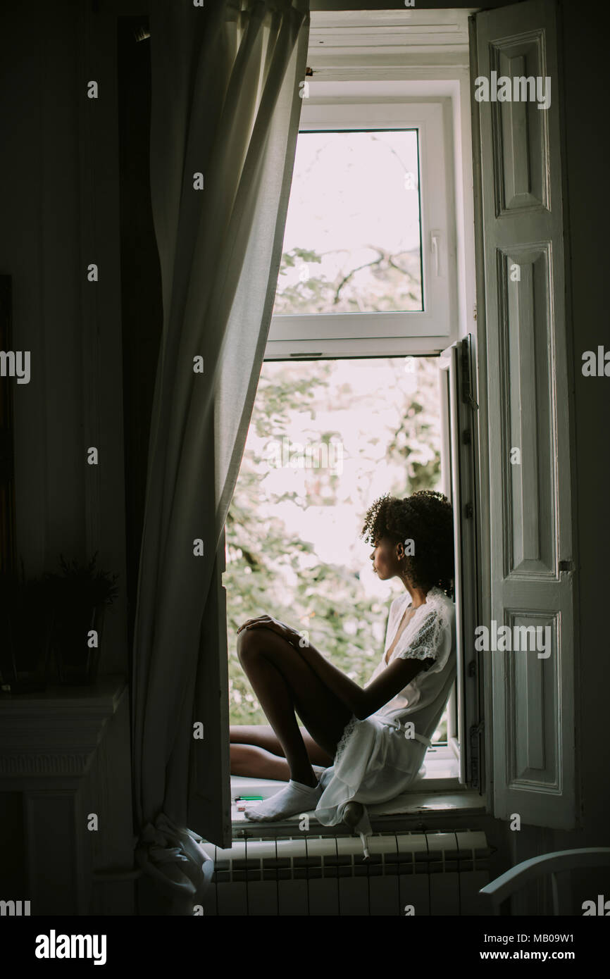 Pretty young black woman sitting on the window in room Stock Photo - Alamy