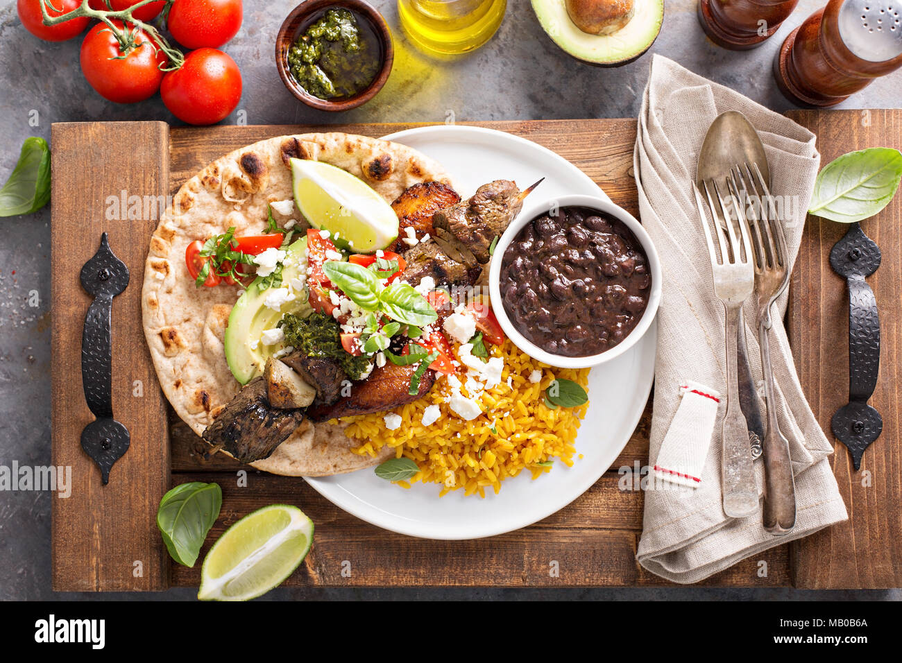 Beef kebab on a flatbread with rice, beans, avocado and fried plantains ...