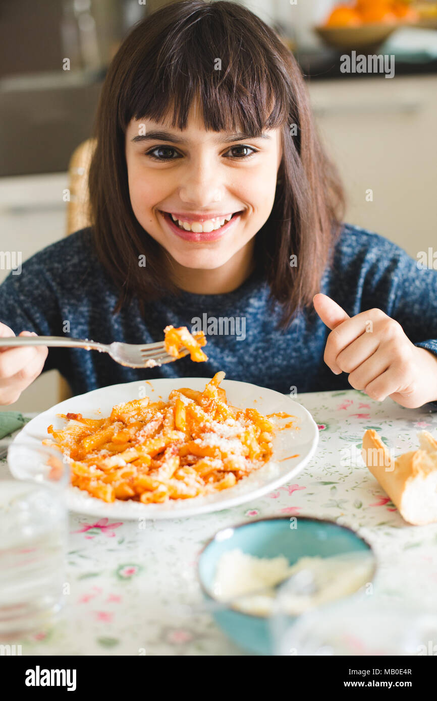 Cute and happy little girl eating pasta with tomato sauce and powdered ...