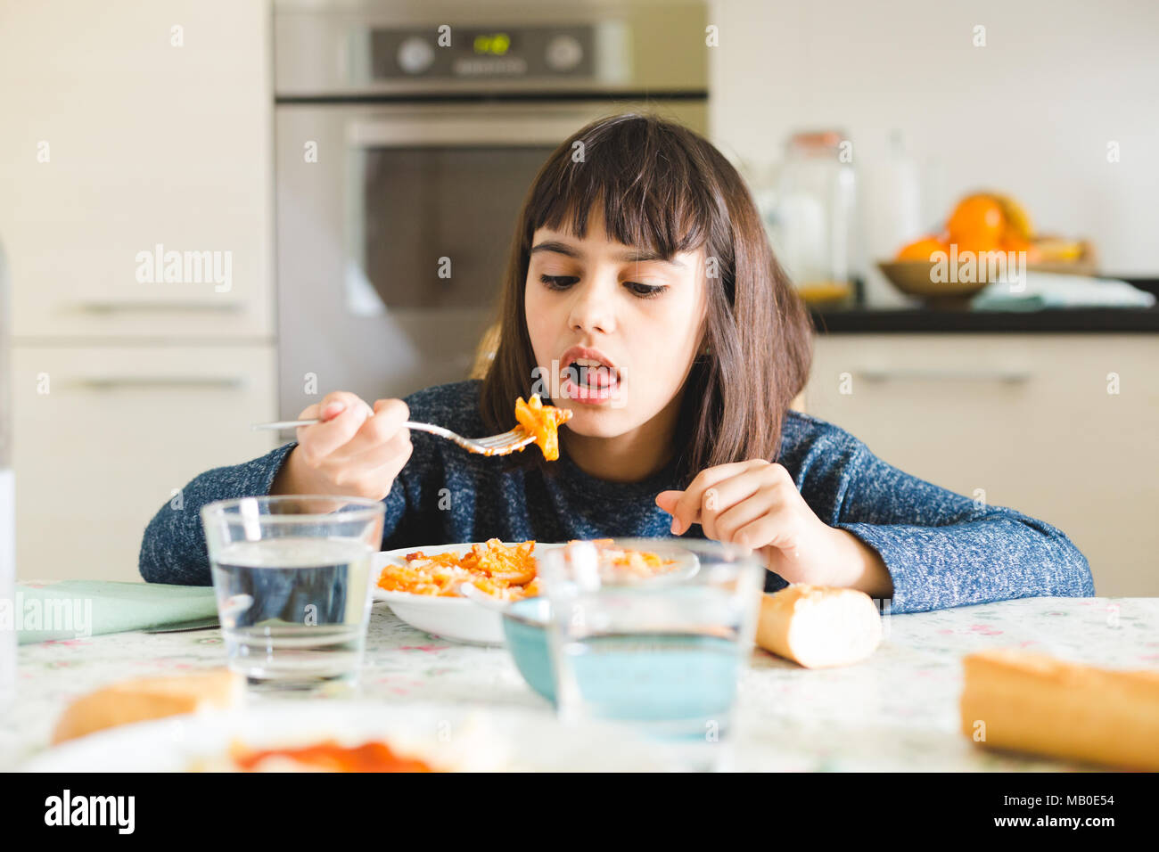 Cute and happy little girl eating pasta with tomato sauce and powdered ...