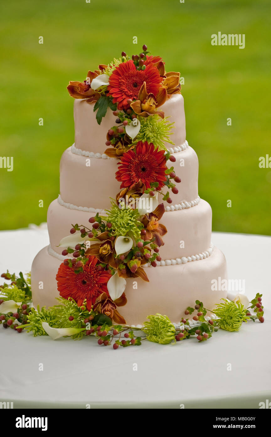 A layered creamy wedding cake wrapping by fresh flowers on a table for ...