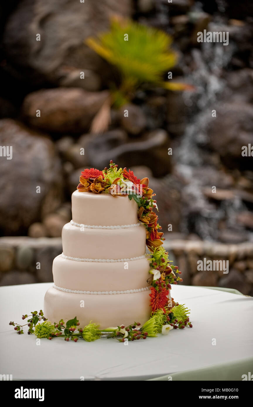 A layered creamy wedding cake wrapping by fresh flowers on a table for ...