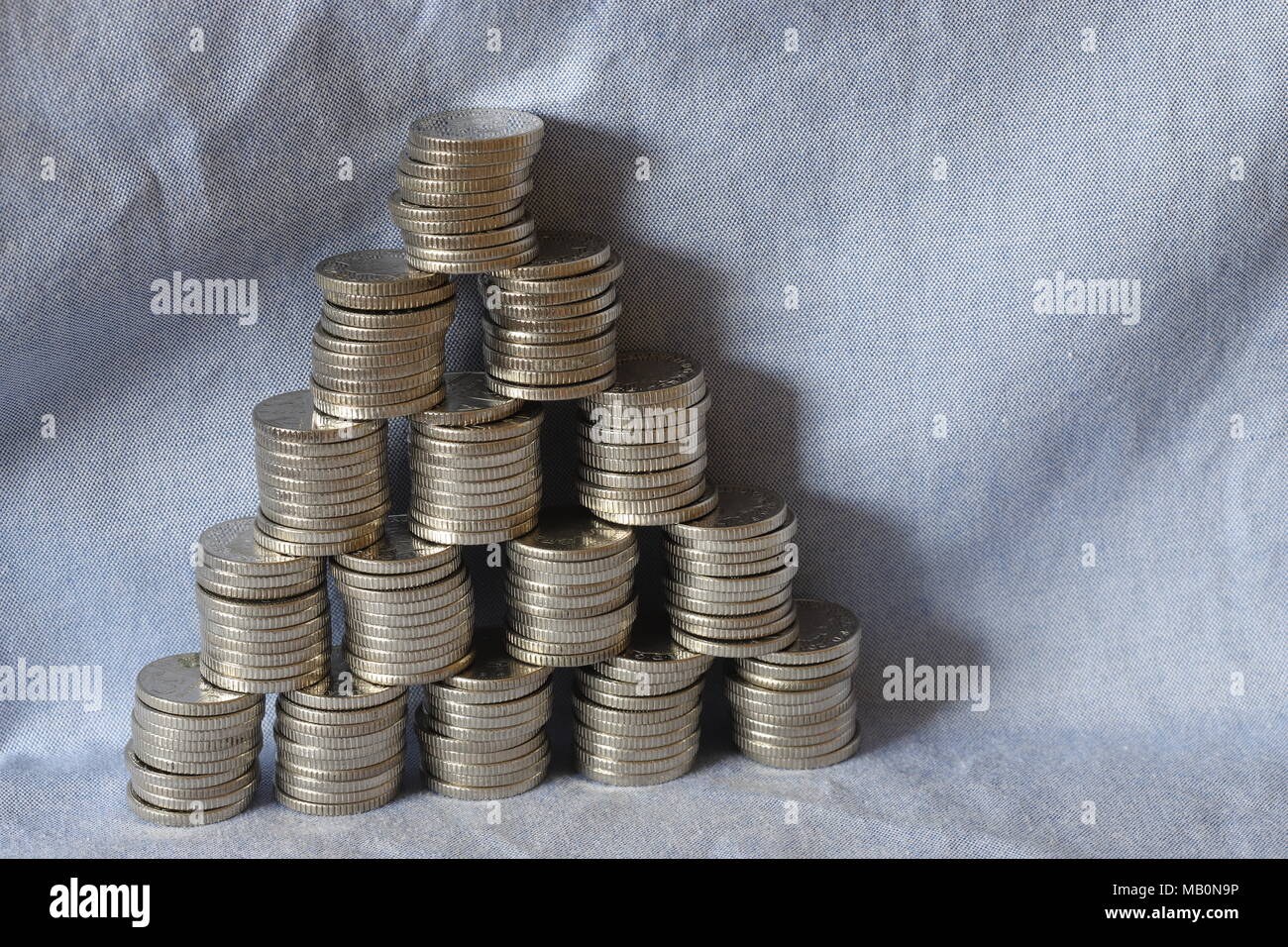 Pyramid stack of current (2018) British 5p coins against a light blue ...