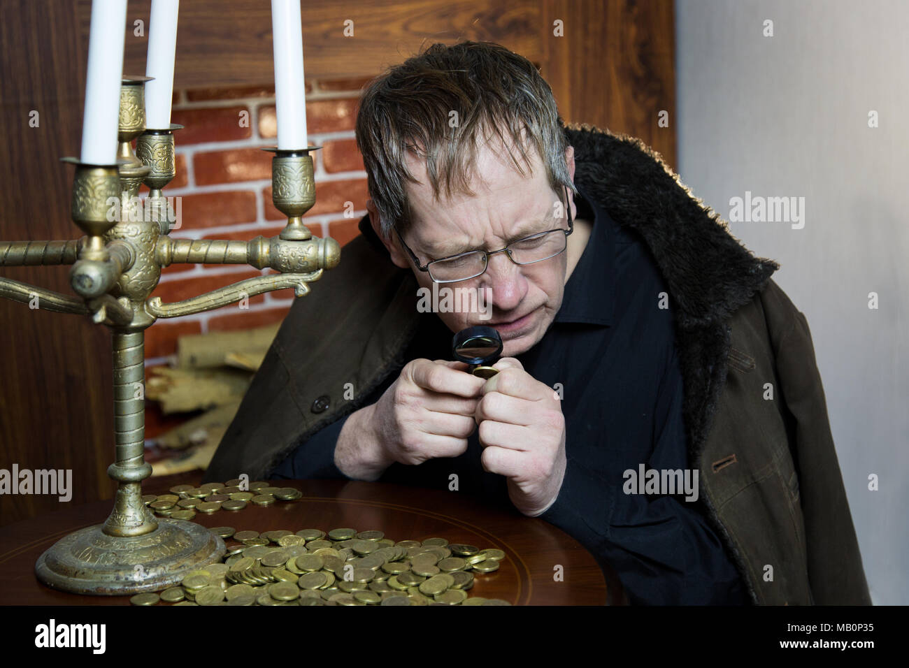 A rich greedy elderly man looks at coins under the light of a burning ...