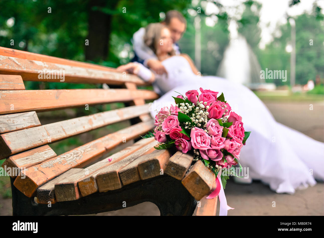 bouquet on wooden bench with bride and groom in the background, focus ...