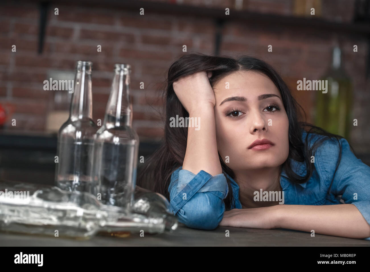 Young female alcoholic social problems sitting at table with empty beer ...