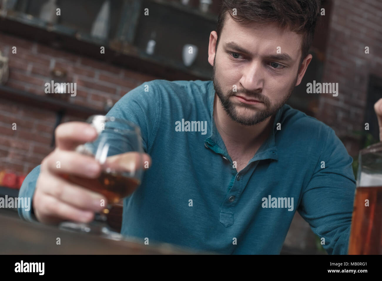 Young man alcohol addiction problems sitting at table looking at glass ...