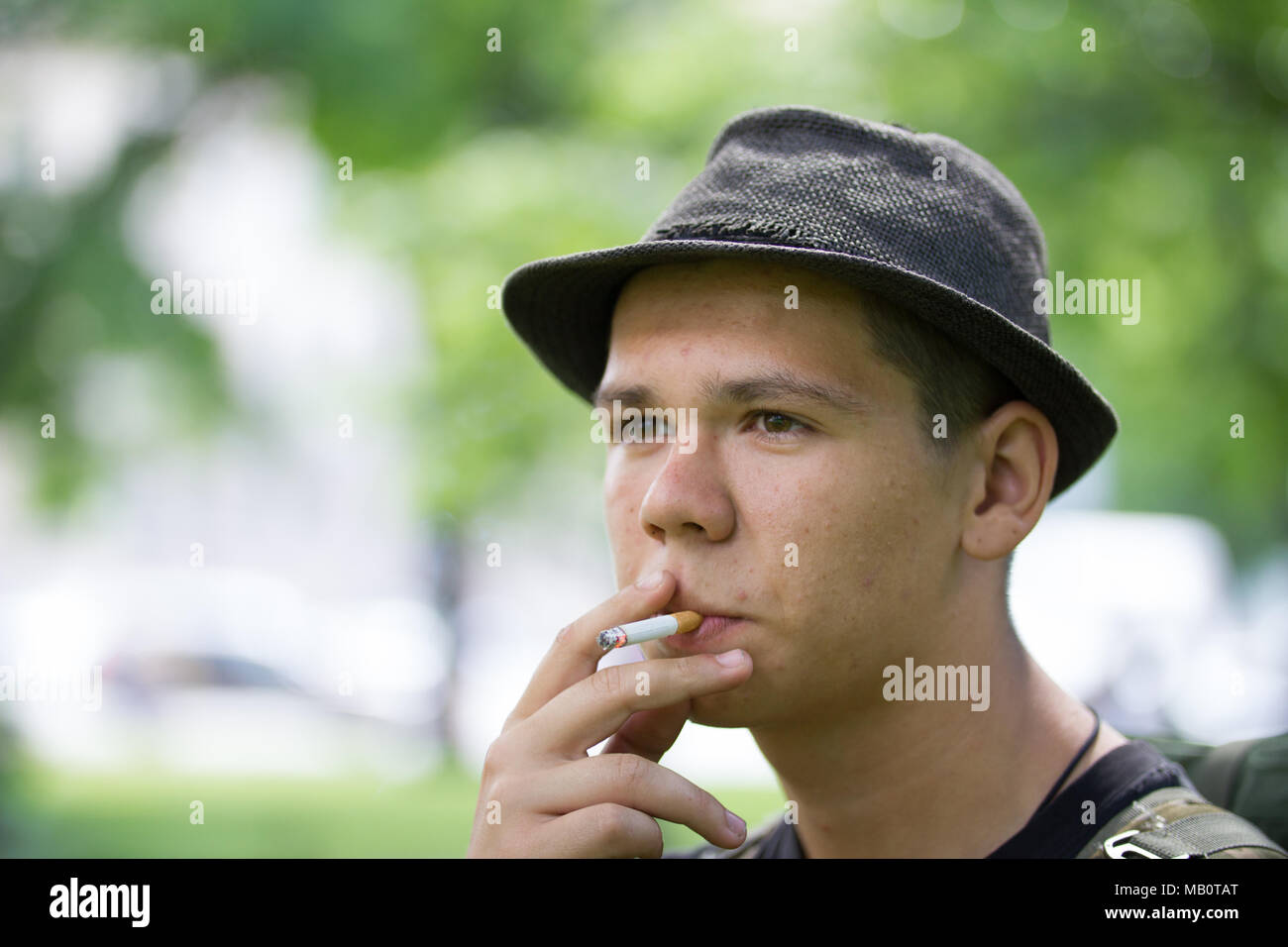 Portrait of young man smoking cigarette in summer park Stock Photo - Alamy