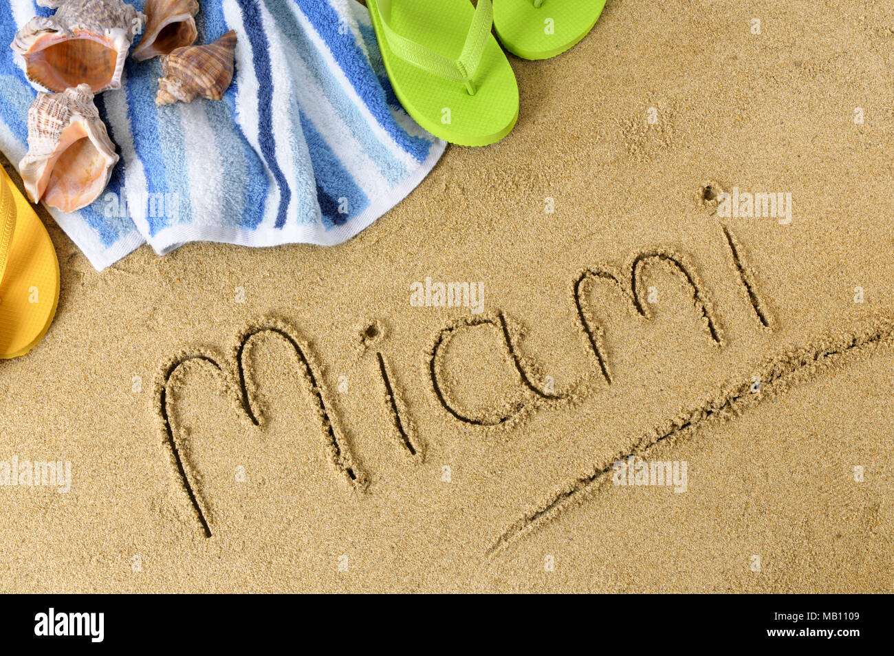 The word Miami written in sand with flip flops and beach towel Stock ...