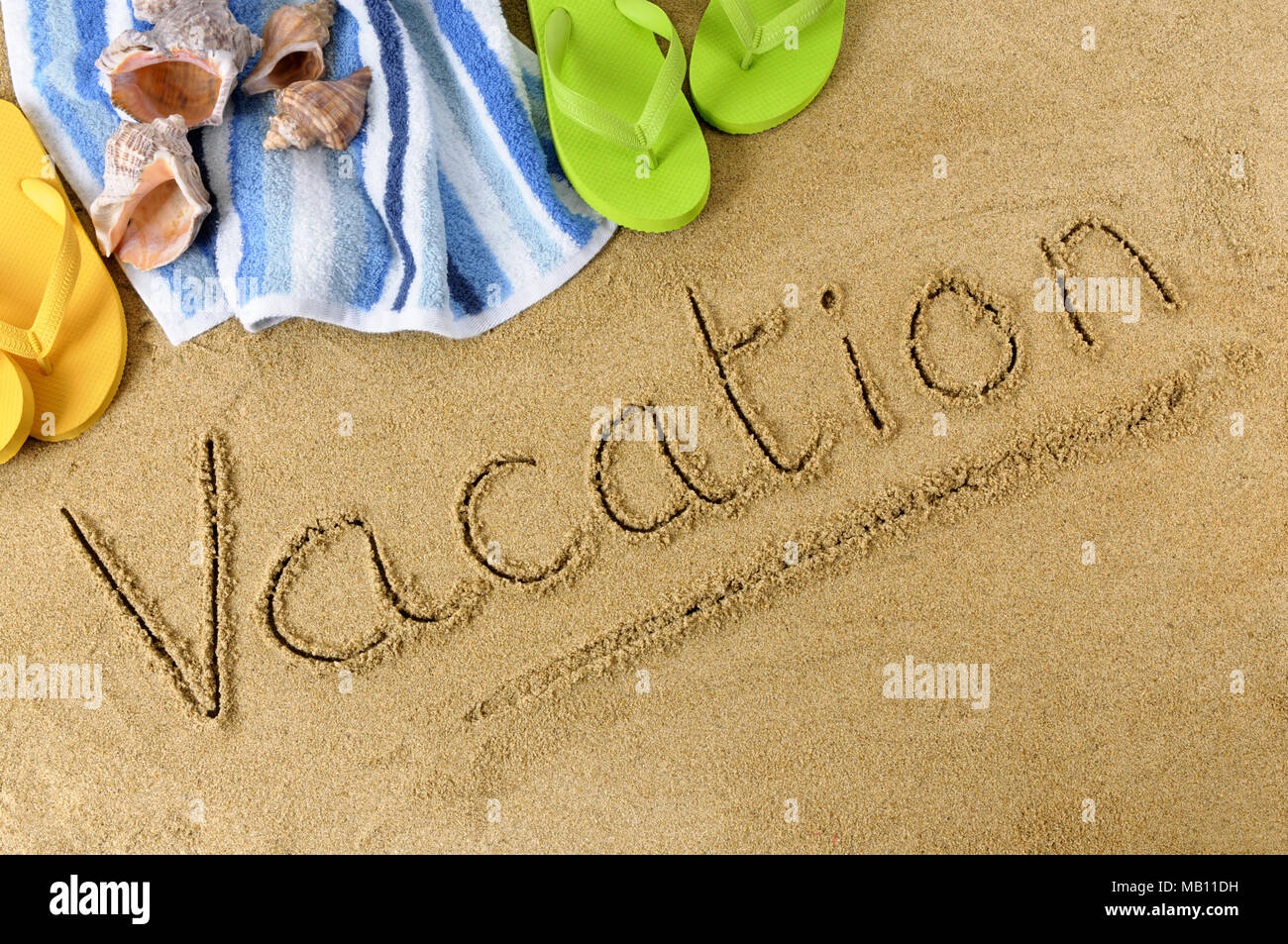 The word vacation written in sand with flip flops and beach towel Stock ...