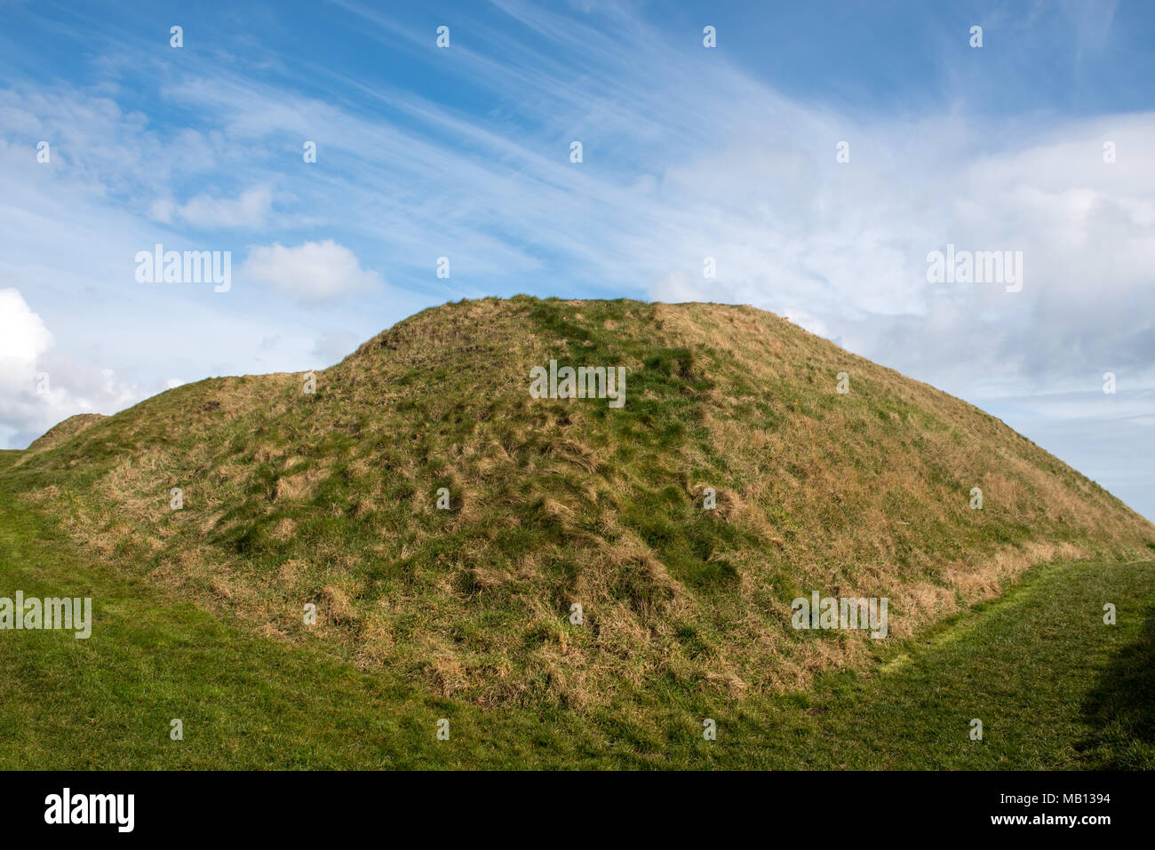 Grassy ancient mound under a dramatic blue sky with wispy clouds ...