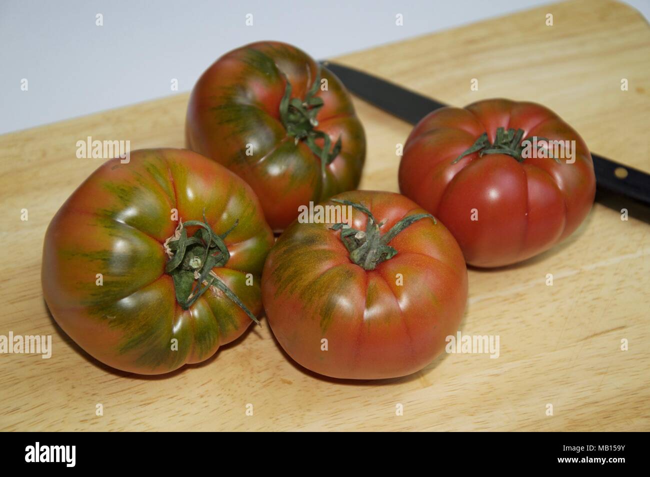 Raf variety tomatoes on a board and with a knife to cut Stock Photo - Alamy