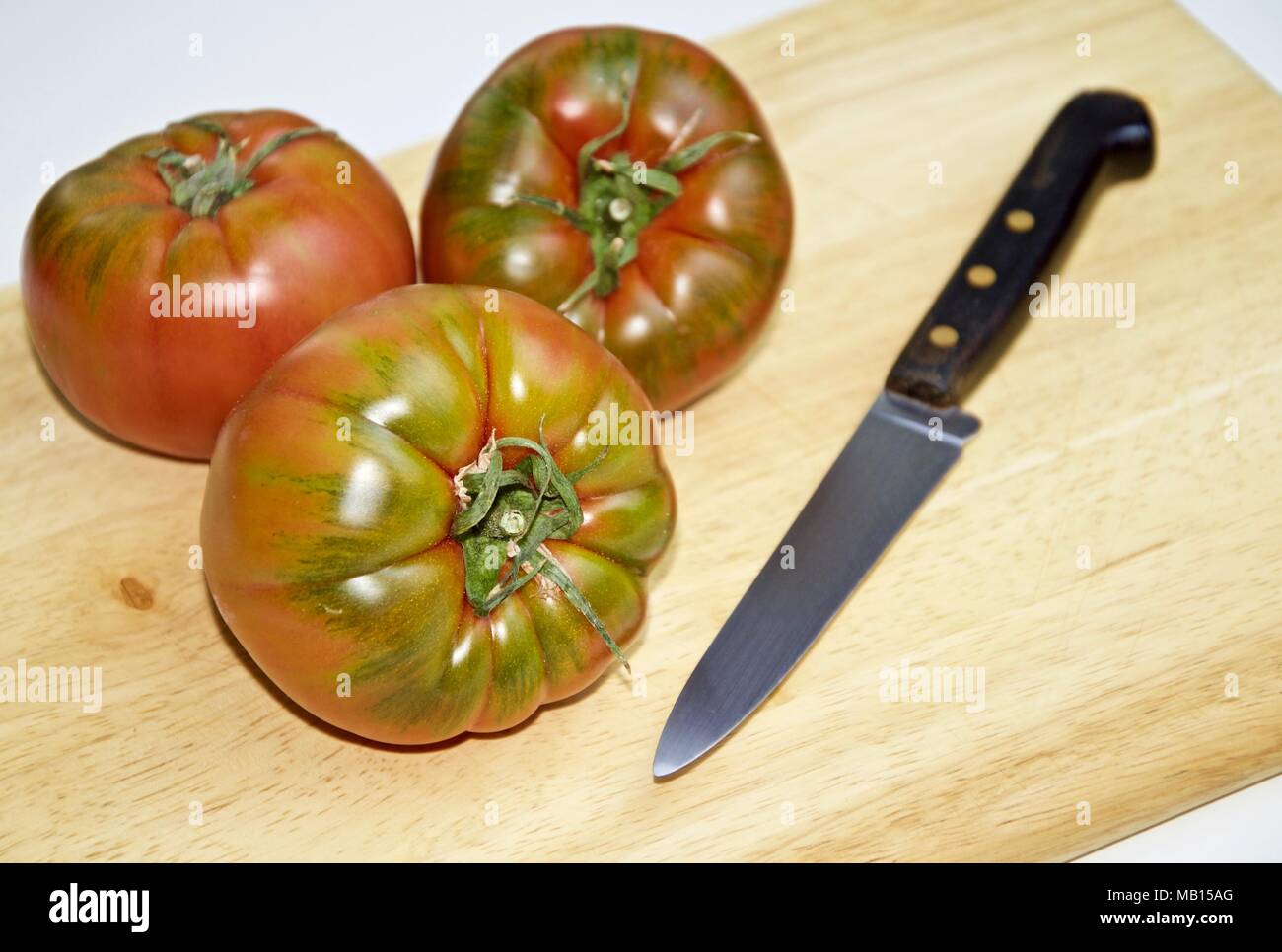 Raf variety tomatoes on a board and with a knife to cut Stock Photo - Alamy