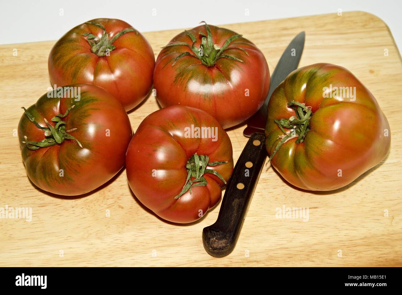 Raf variety tomatoes on a board and with a knife to cut Stock Photo - Alamy