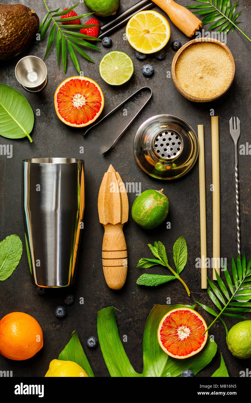 Cocktail making bar tools, shaker, tropical fruits and leaves on a dark ...
