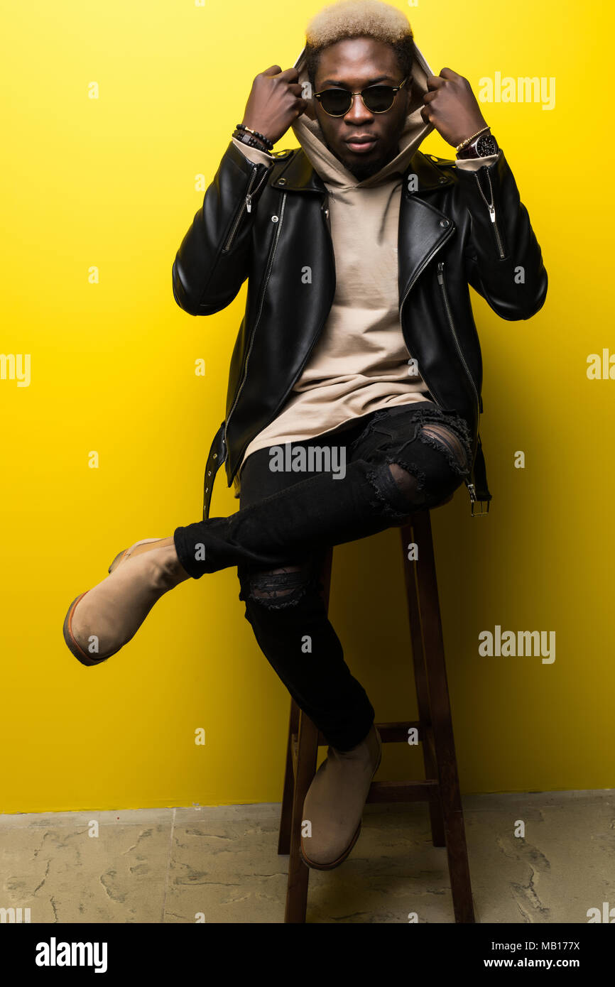 Happy african man sitting in a chair isolated over yellow background ...