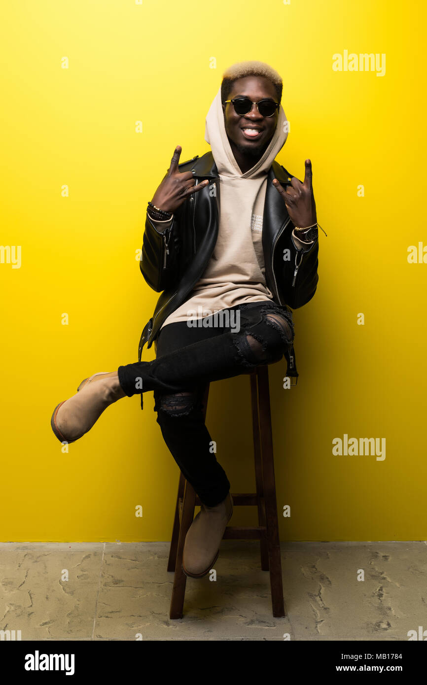 Happy african man sitting in a chair isolated over yellow background ...