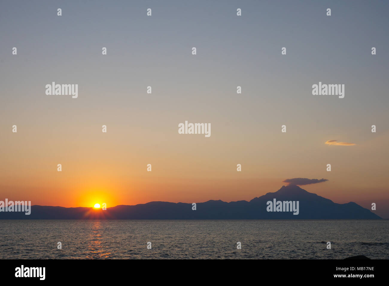 Sunset at the sea. Sun falling down behind mountain Stock Photo - Alamy