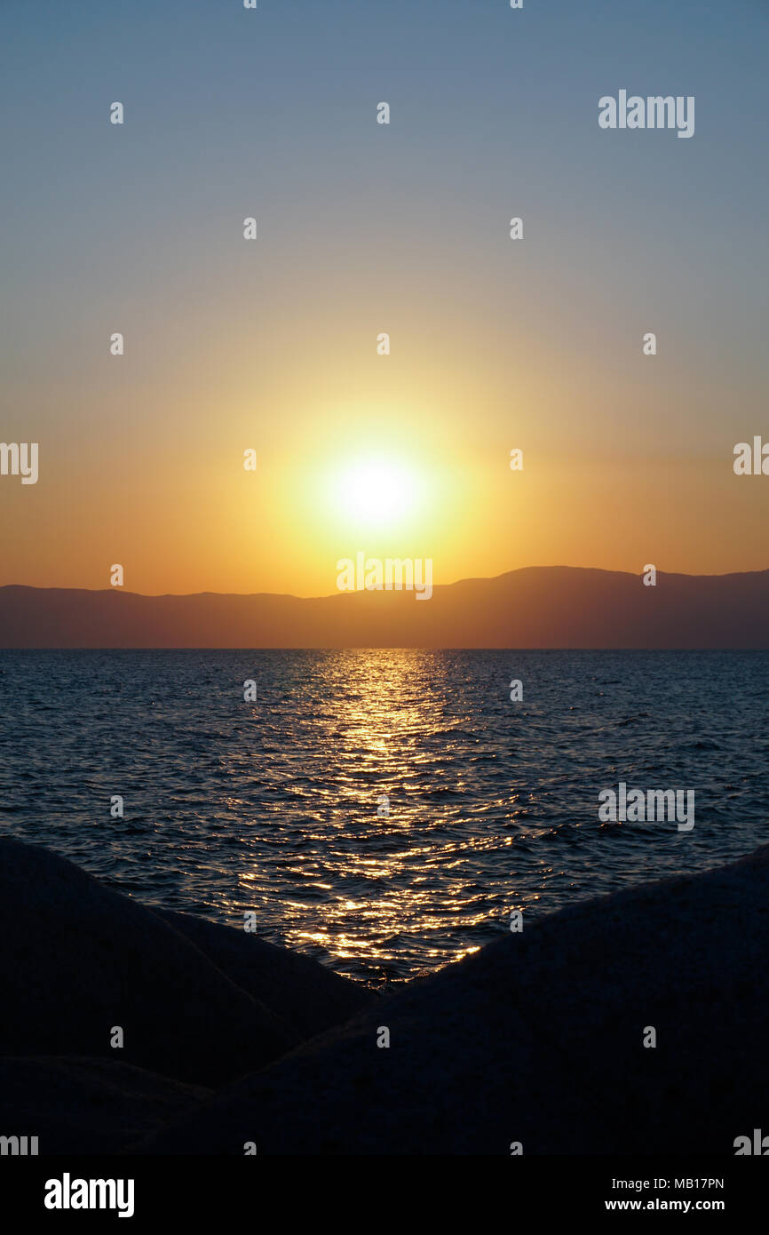 Sunset at the sea. Sun falling down behind mountain Stock Photo - Alamy