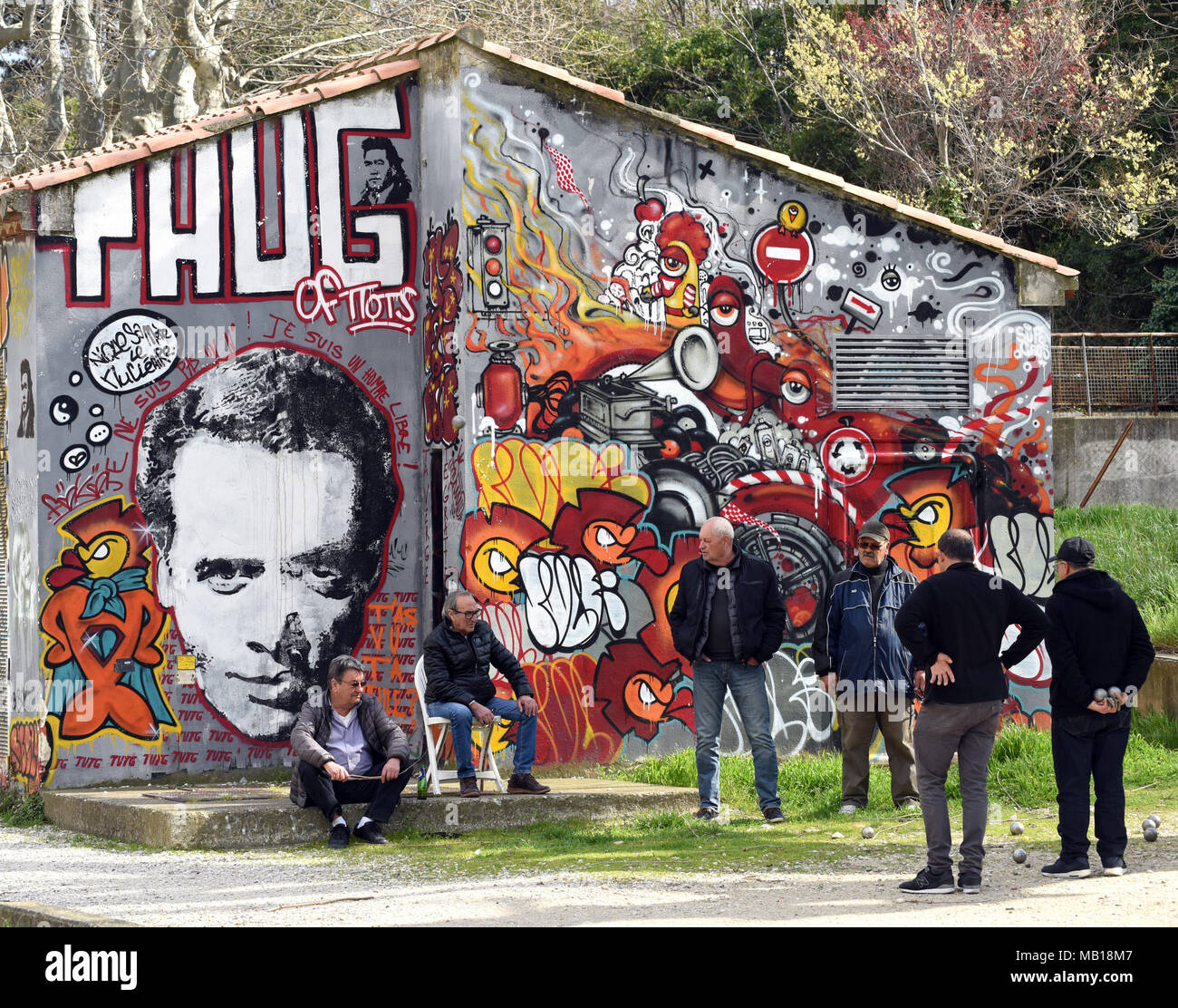 French men playing boules in front of building covered in graffiti in ...